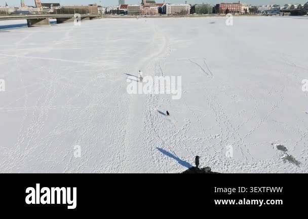 Aerial drone view shows two adults and a dog crossing frozen Daugava ...