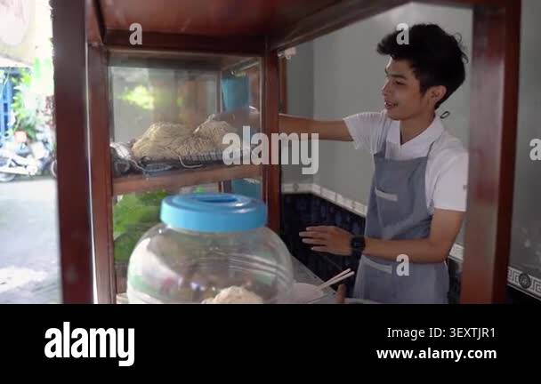 Smiling worker in apron serves and prepares pastry inside small food ...