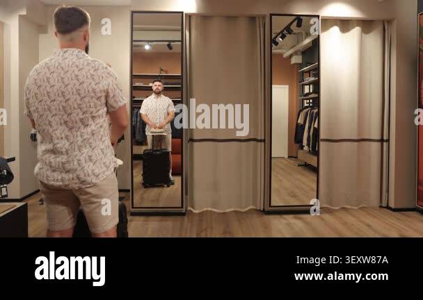 Male customer looking in the mirror while trying on a summer outfit ...
