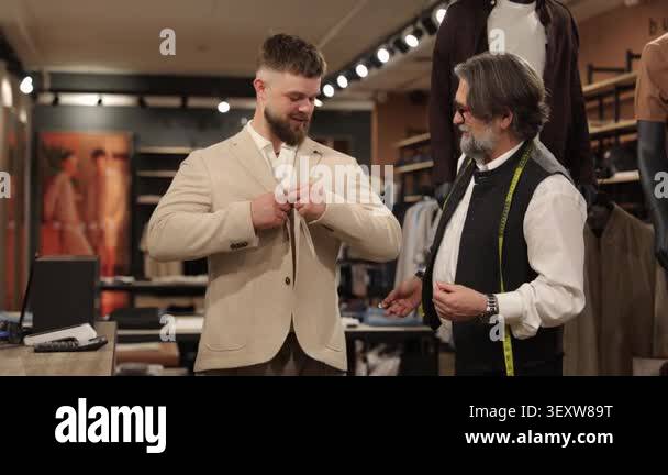 Experienced tailor advising a happy client trying on a new jacket in a ...
