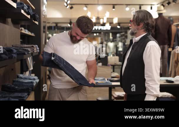 Smiling man examining a pair of jeans with the help of an experienced ...