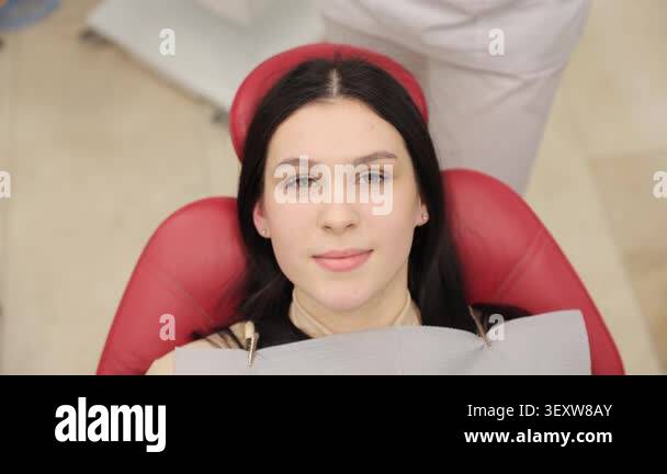 Pretty young woman sitting in a dental chair, smiling and looking at ...