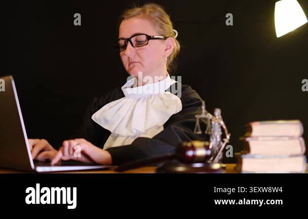 Serious woman judge in a robe typing on a laptop computer at her desk ...