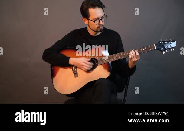 Young handsome talented guitarist in glasses playing guitar in studio ...