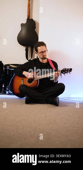 Young brunette musician in glasses playing guitar in his music studio ...