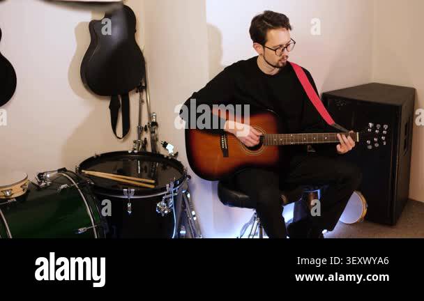 Young brunette musician in glasses playing guitar in his music studio ...