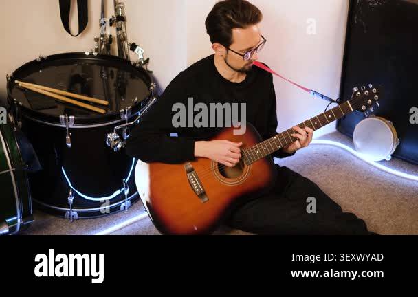 Young brunette musician in glasses playing guitar in his music studio ...