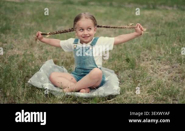 Playful little girl with braids holding her hair and smiling while ...