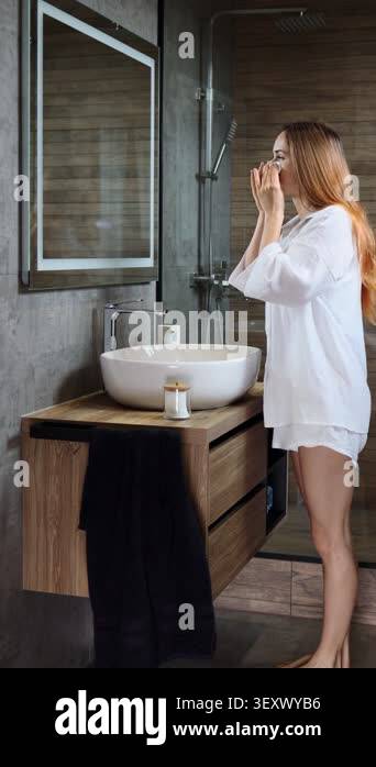 Young beautiful woman in white robe cleaning her face with cotton pad ...
