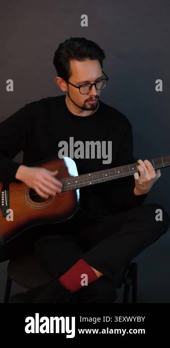 Young brunette musician in glasses playing guitar in his music studio ...