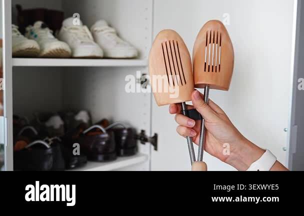Wooden shoe trees are displayed in hand against a wardrobe filled with ...