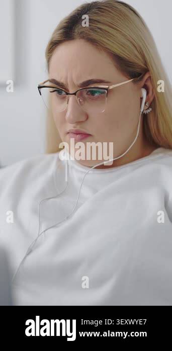 Woman looks at laptop with a puzzled expression in a bright room during ...