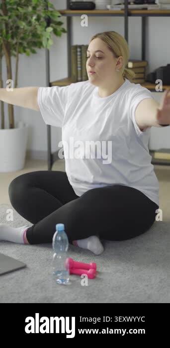 Woman sits on floor practicing fitness movements using a laptop at home ...