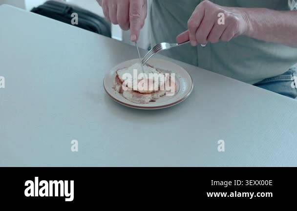 Man cuts toast with knife and fork at table. Hands steady, focused on ...