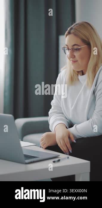 Woman sits at home working on a laptop while looking at the screen and ...