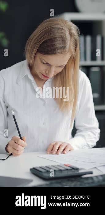 Woman works at a desk with papers and a calculator while showing ...