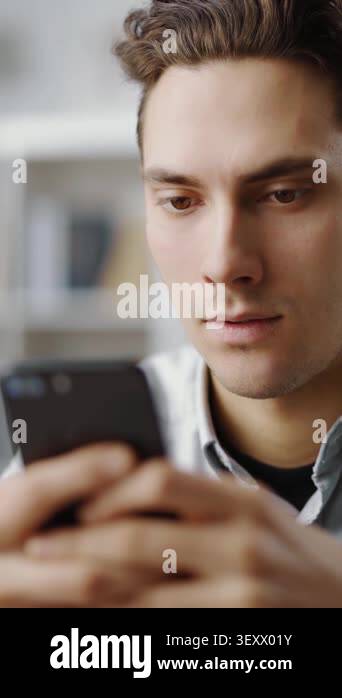 A man looks at his smartphone while smiling and scrolling through ...