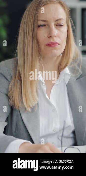 Woman in a gray suit looks sleepy while working in an office. She yawns ...