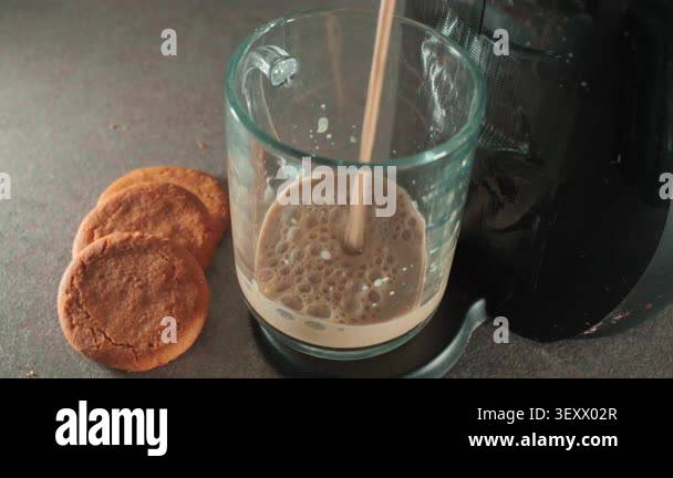 Empty glass sits beside cookies on a table. Liquid pours into glass ...