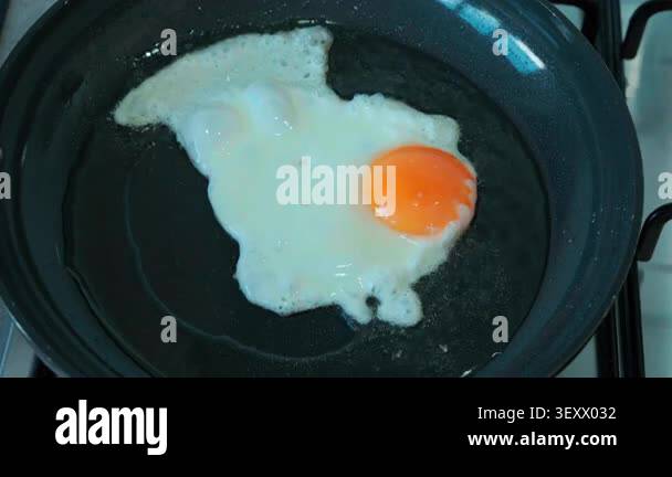 Fried egg sizzles gently in black skillet. Yolk gleams bright, white ...