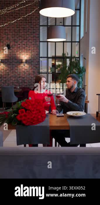 Romantic couple enjoying dinner with red roses and wine in stylish ...