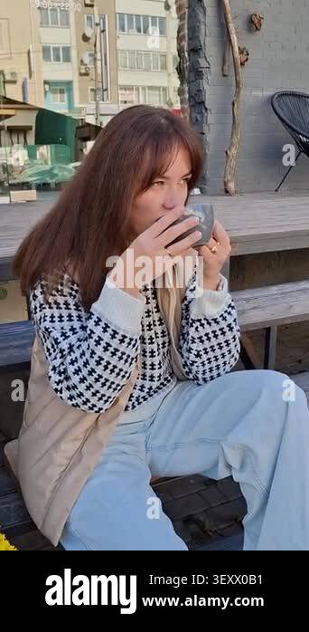 Beautiful woman sits on a wooden bench holding a cup of coffee at a ...
