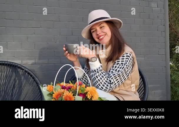 A woman sits at a round table outside and holds a cup of coffee ...
