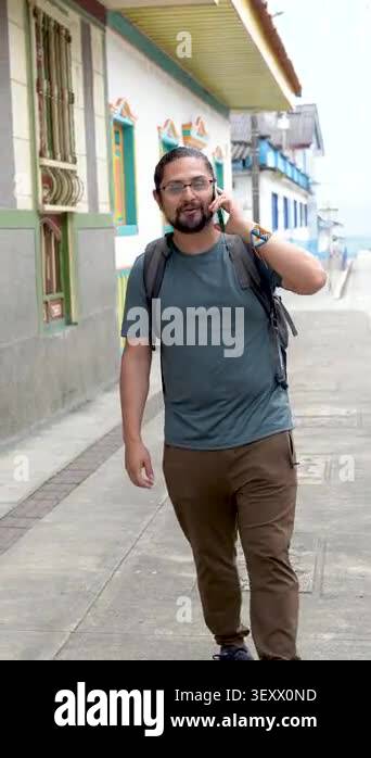 Smiling male tourist with a backpack talks on his smartphone while ...