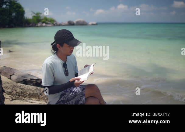 Man Reading a Book While Sitting on Driftwood on a Beautiful Beach ...