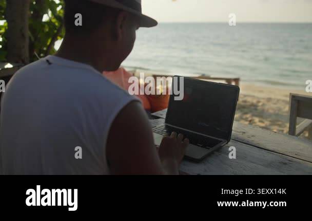 Digital Nomad Working on a Laptop by the Ocean at Golden Hour ...