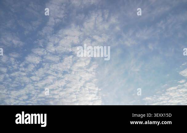 Textured altocumulus clouds slowly drift across a bright blue sky in a ...