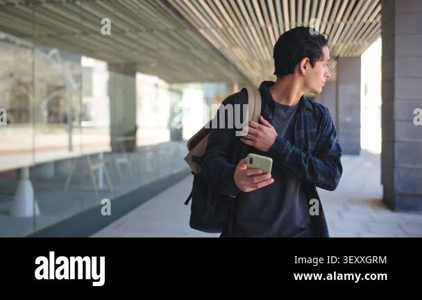 Portrait of young man walking using mobile phone and smiling at camera ...