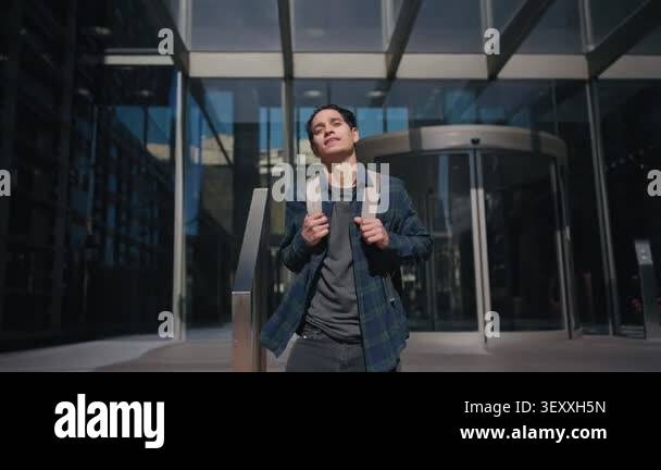 Young latin man walking out of modern office building carrying backpack ...