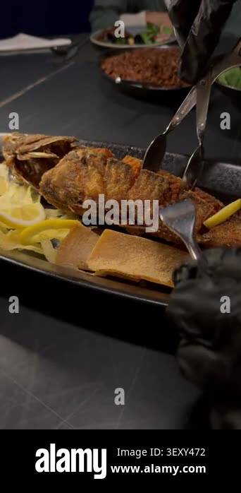 Waiter cutting a whole crispy fried fish at a luxury restaurant table ...
