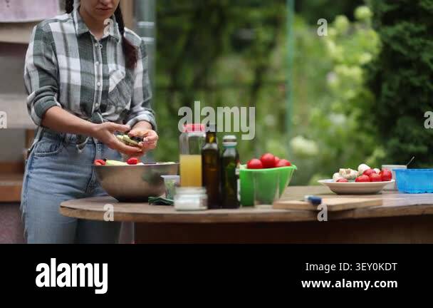 Young woman in a plaid shirt slicing fresh zucchini and adding it to a ...
