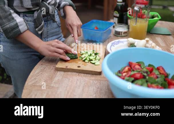 Close-up of a womans hands cutting a fresh cucumber on a wooden board ...