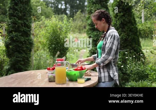 Young woman with braided hair preparing a fresh salad on a wooden table ...