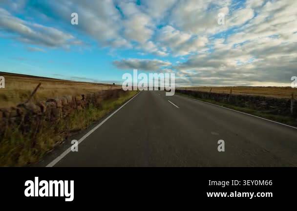 Car driving along long country road bordered by stone fences and open ...