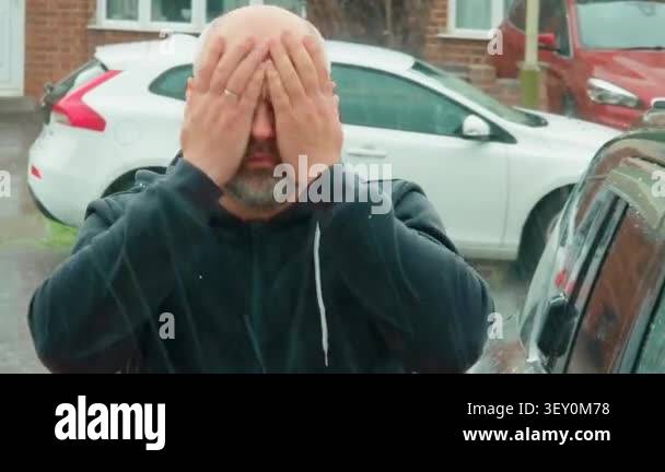 Man wiping rain water from face during heavy downpour in residential ...