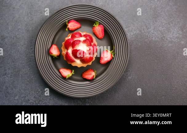 Strawberry tart served on a dark plate with strawberries on a textured ...