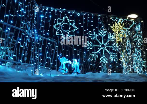 Bright garlands shine in the night as snow covers the ground. The ...