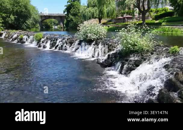 Arnoia river flowing over a stone weir with a historic bridge in the ...