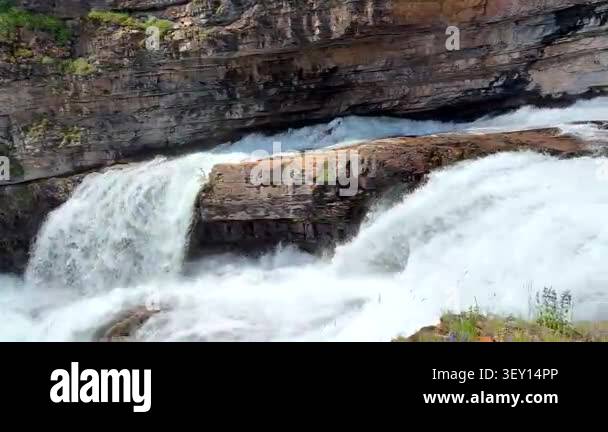 Water rushes down the rocks of a large waterfall. Sunlight shines on ...