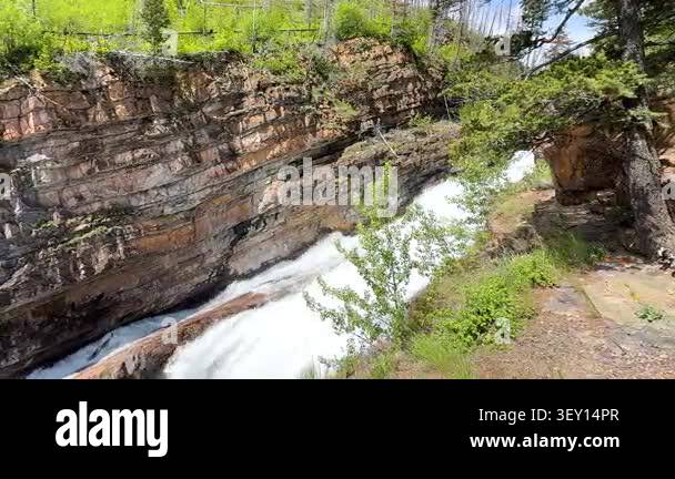 Water rushes down the rocks of a large waterfall. Sunlight shines on ...