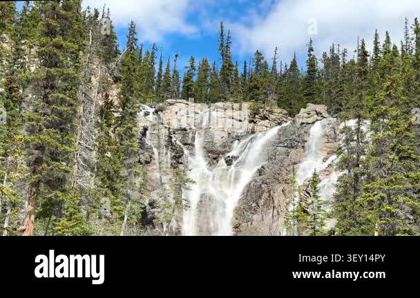 Water rushes down the rocks of a large waterfall. Sunlight shines on ...