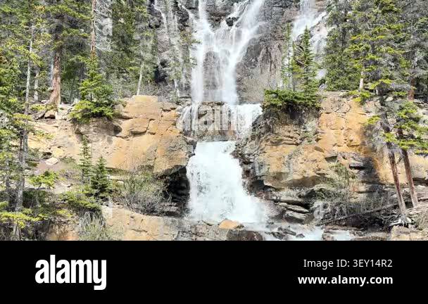 Water rushes down the rocks of a large waterfall. Sunlight shines on ...