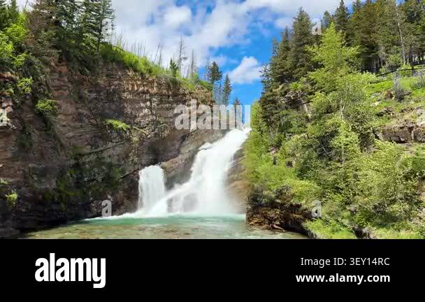 Water rushes down the rocks of a large waterfall. Sunlight shines on ...