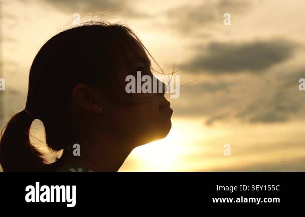 Low angle shot of a little girl looking up at the cloudy sky with wind ...