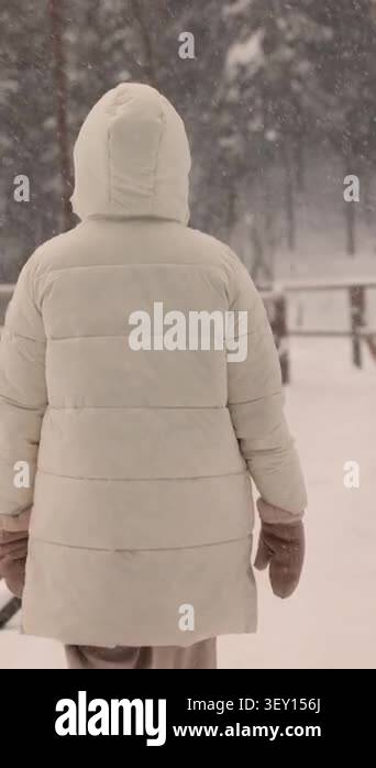 Back view of woman wearing beige winter outfit walking across wooden ...