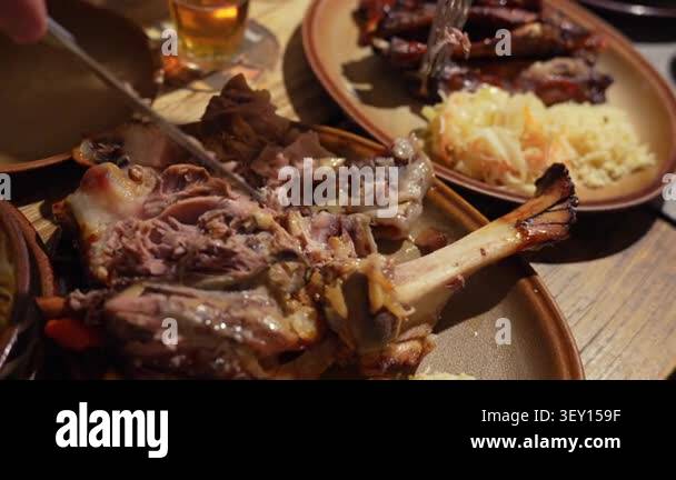A hand carves Czech pork knuckle off the bone on a rustic ceramic plate ...